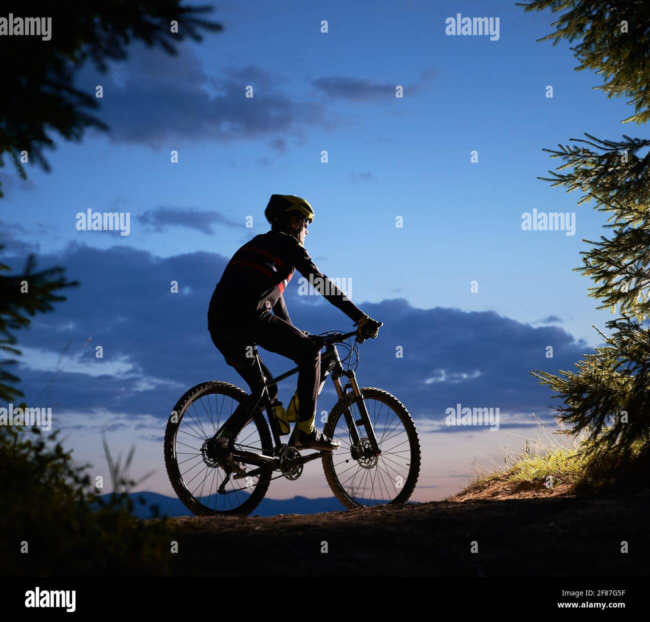 Side view of man riding bike under blue evening sky with clouds ...