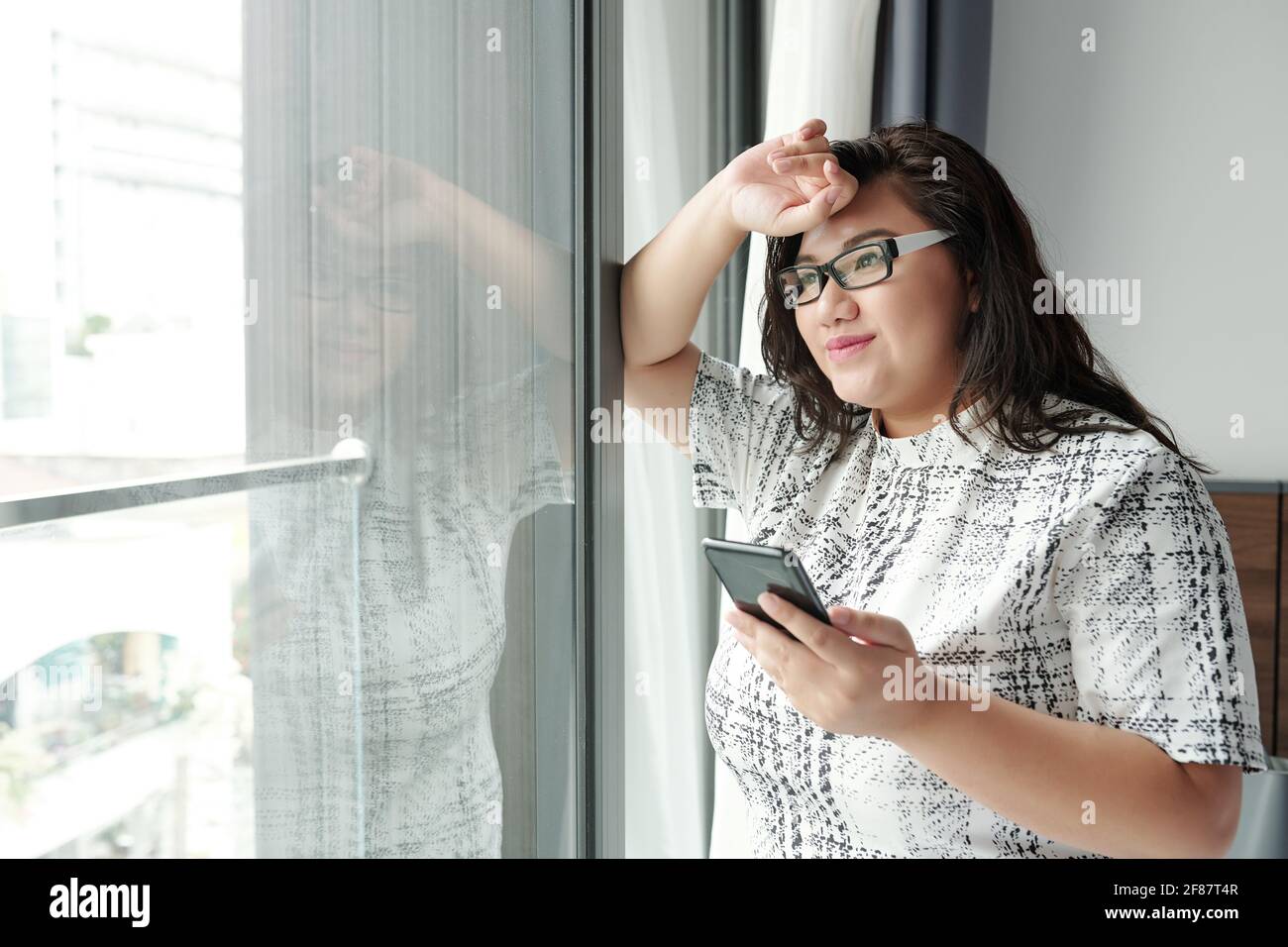 Smiling pretty young woman looking through window and receiving text ...