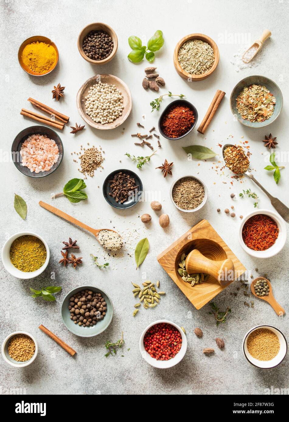 Various dry spices in small bowls and raw herbs flat lay on grey ...