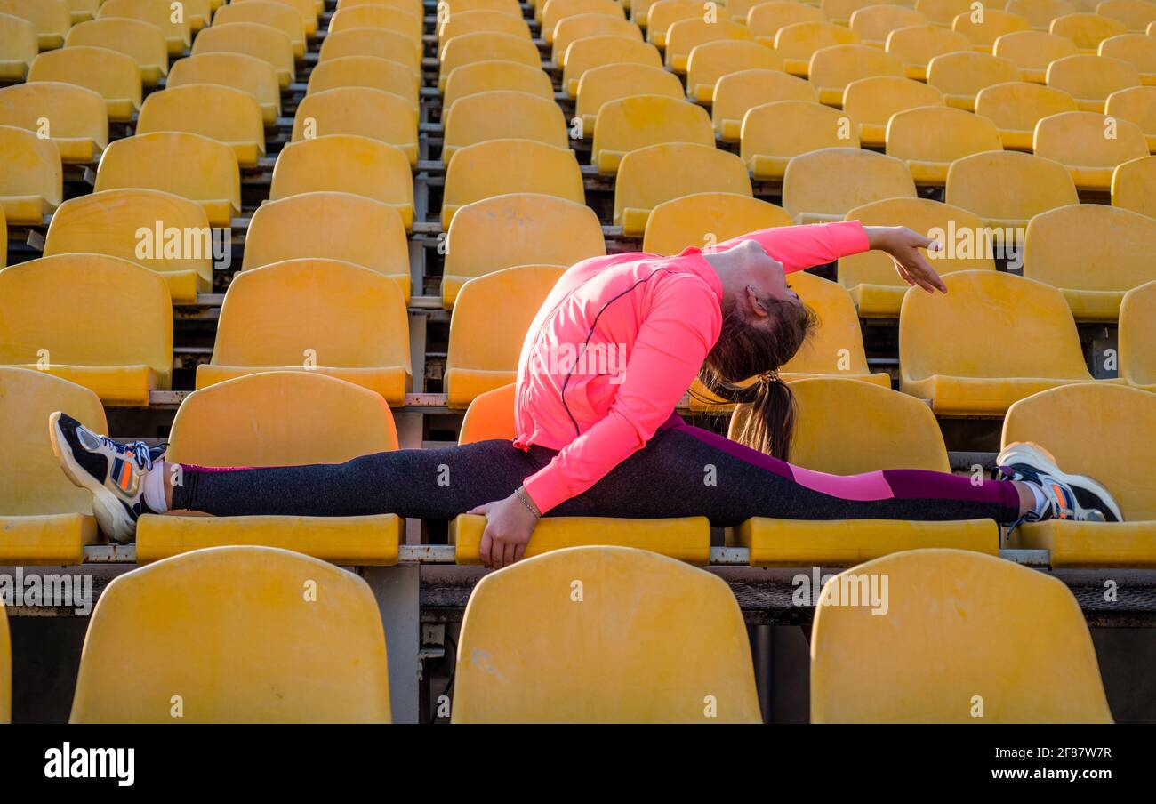 girl kid training sport outside on stadium tribune sit in split ...