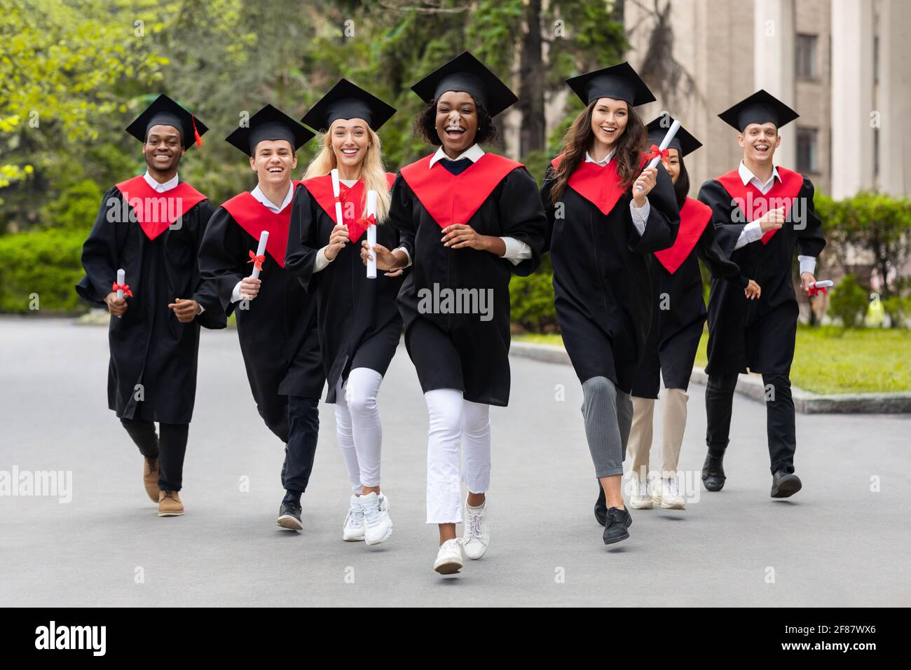 Cheerful multiracial students in graduation costumes walking by ...