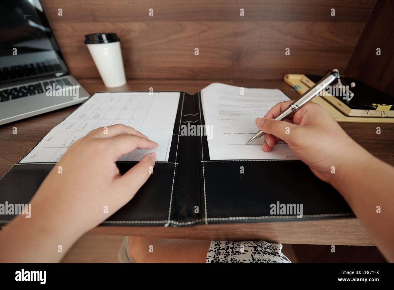 Close-up image of businesswoman signing agreement in leather folder on ...