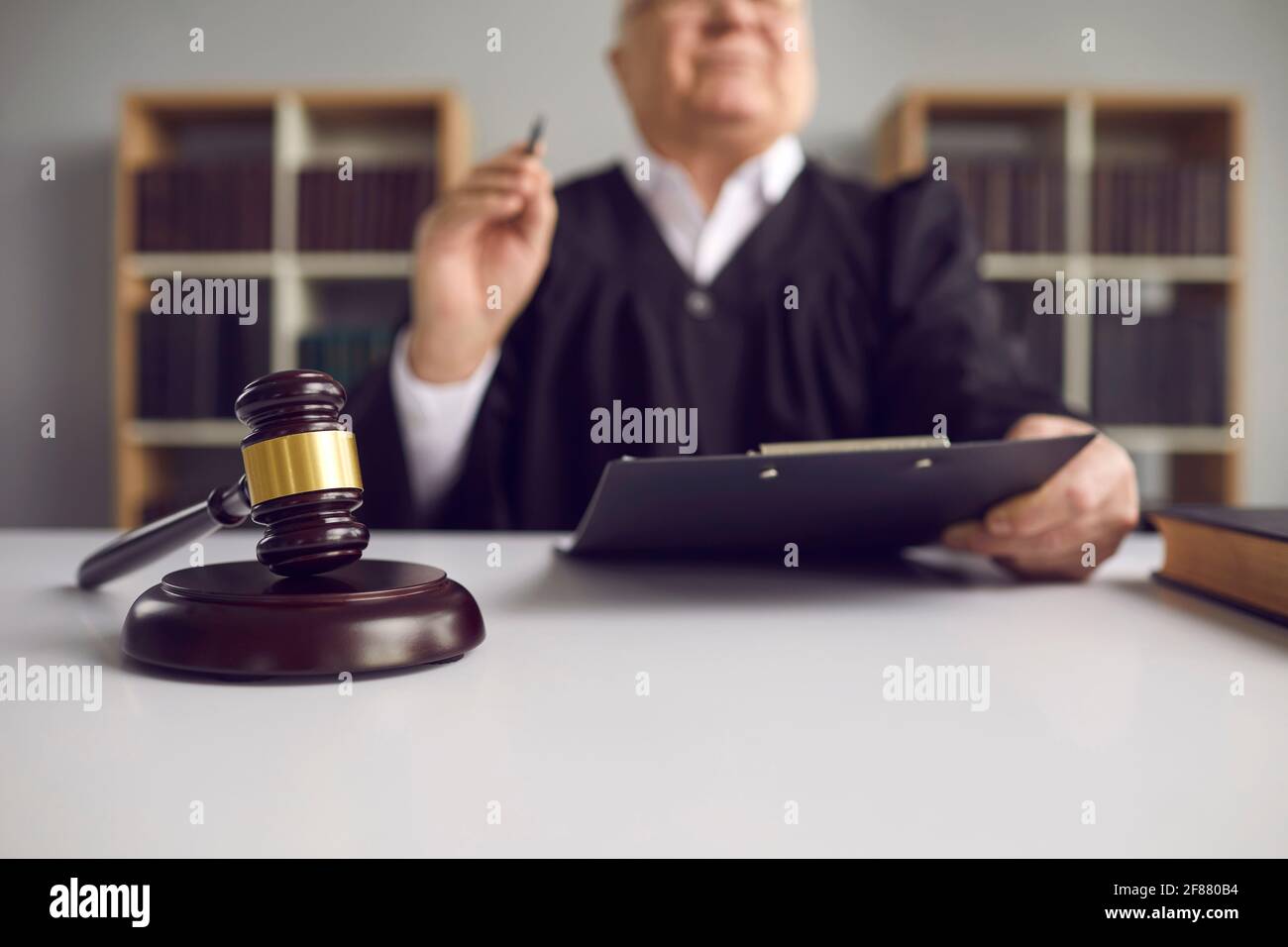 Senior judge with pen and clipboard sit at table shot with focus on ...