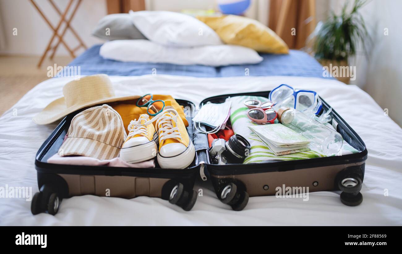 Open suitcase packed for holiday on bed at home, coronavirus concept ...