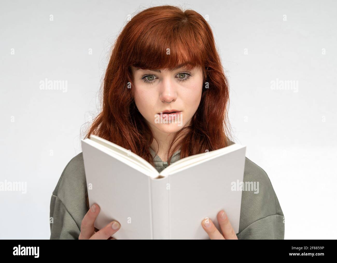 Portrait of a woman with red hair infront of white background reading a ...