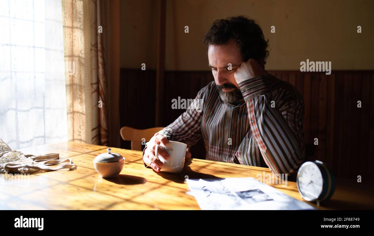 Portrait of unhappy poor mature man reading newspapers indoors at home ...