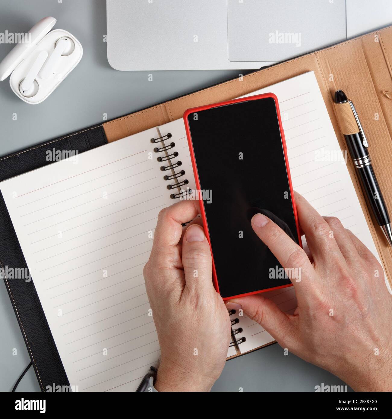 Man writing in agenda and using cell phone on a grey office desk top ...