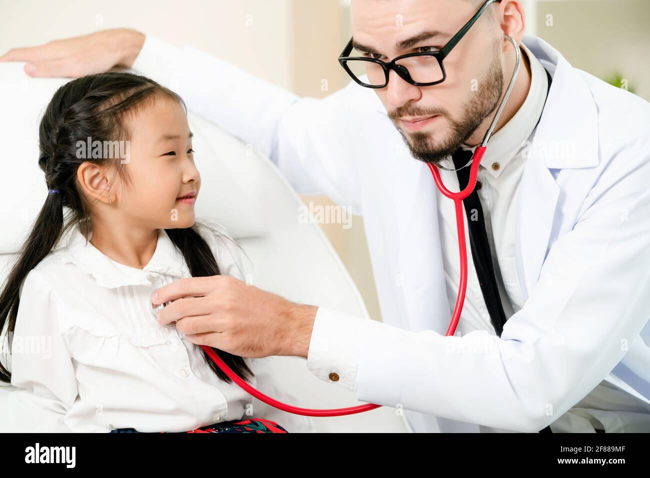 Young male doctor examining little kid in hospital office. The kid is ...