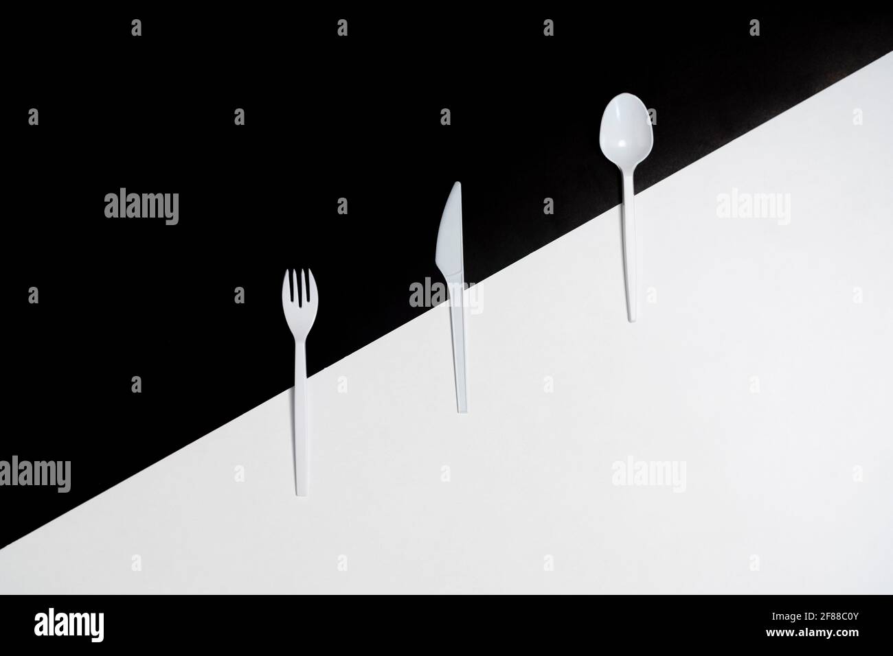 Plastic fork, knife and spoon on diagonally divided black and white ...