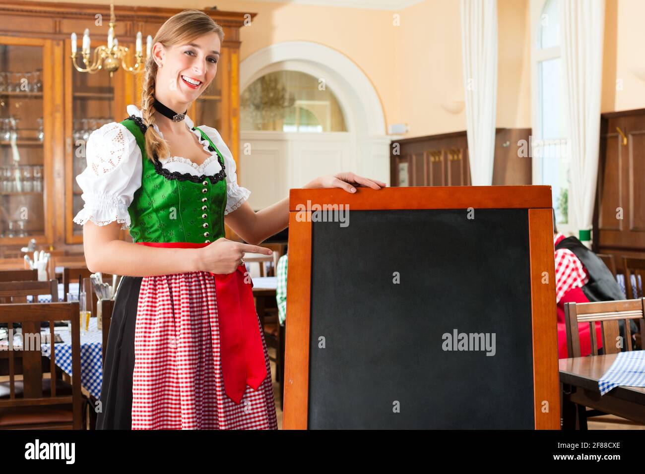 Female Innkeeper in traditional Bavarian clothes in pub with display ...