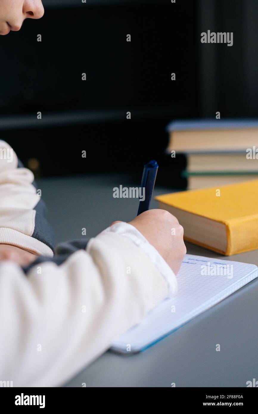 Close-up of pupil boy writing notes in paper workbook sitting at desk ...