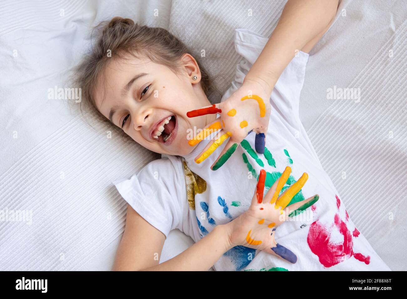 Painted smiles on the palms of a little girl in a T-shirt with colored ...