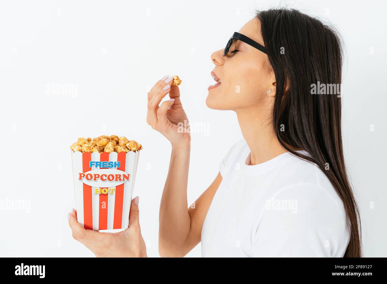 Young woman wearing 3D glasses eating popcorn out of paper bag while ...