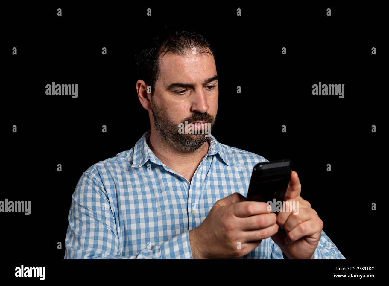 Bearded man in plaid shirt using a mobile isolated on a black studio ...