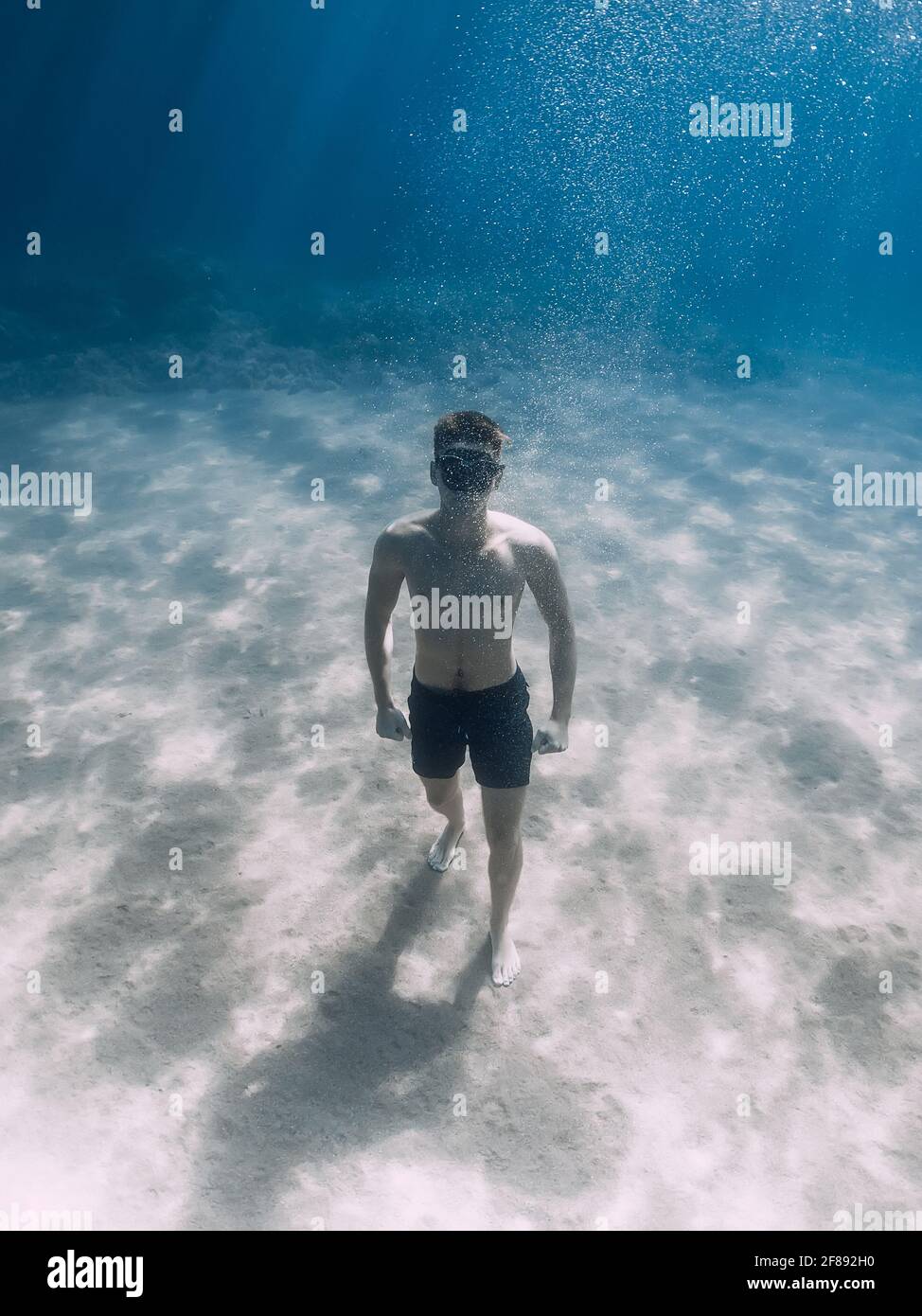 Sporty man freediver stay on sand bottom underwater in tropical sea ...