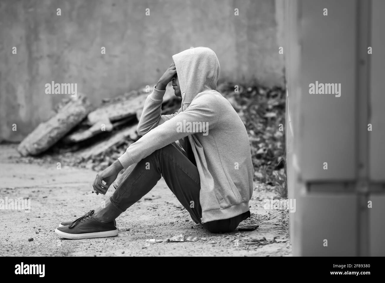 Male junkie with syringe and drugs sitting near wall outdoors Stock ...