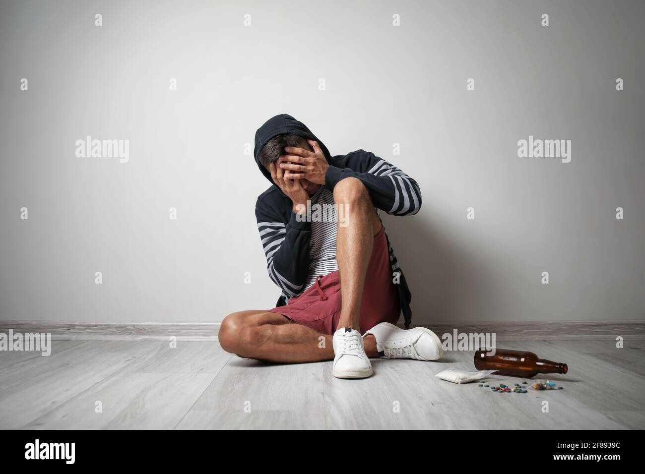 Male junkie with drugs and alcohol sitting on floor Stock Photo - Alamy