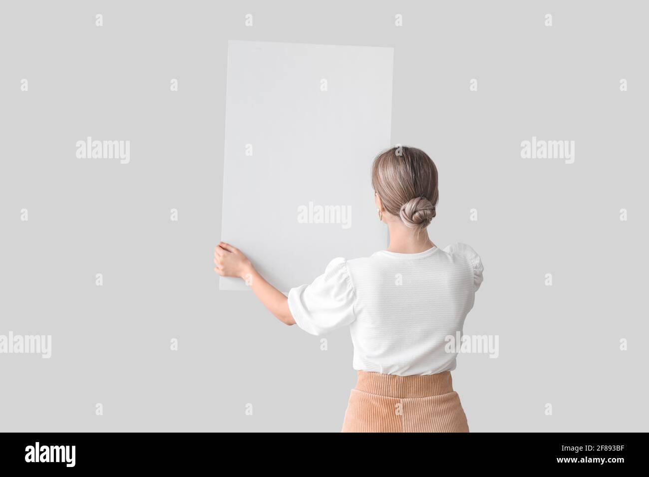 Beautiful young woman with blank poster on light background, back view ...