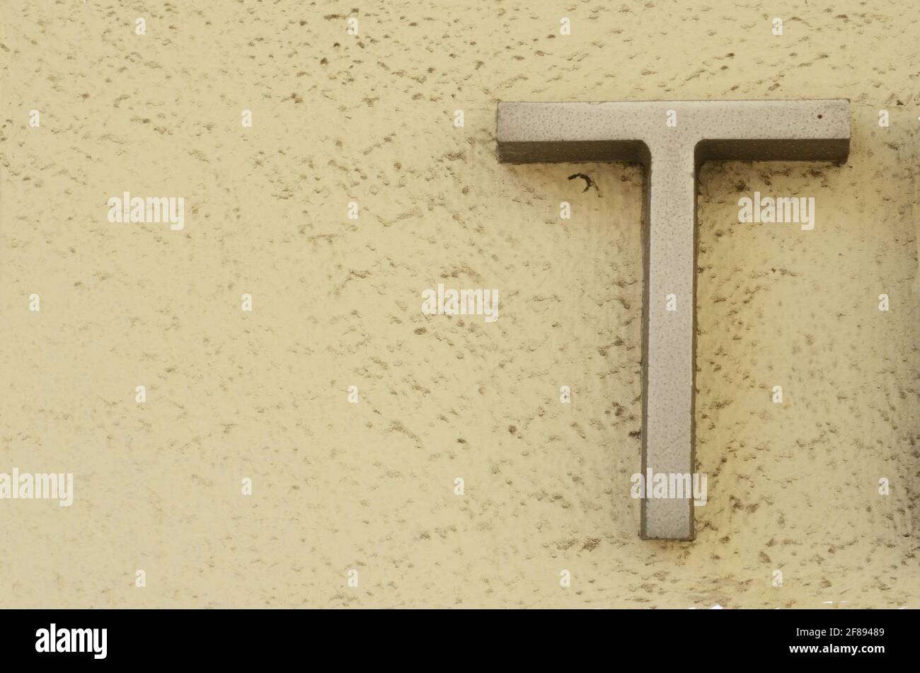 Raised sliver letter T on beige stucco wall. The gem is worn, faded ...