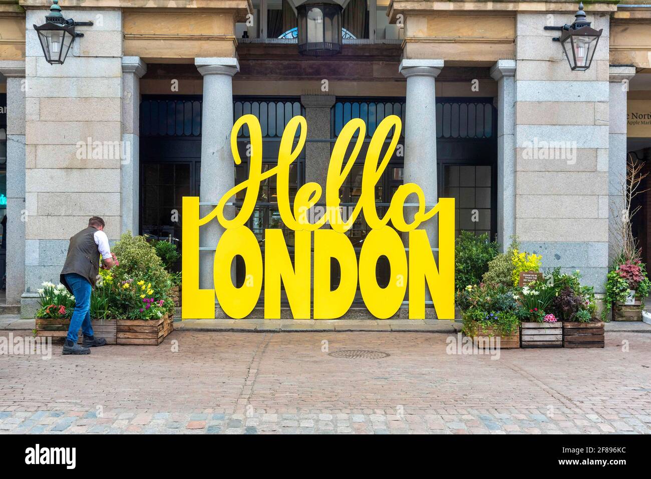 A man plants flowers next to a large yellow sign saying ‘Hello London ...