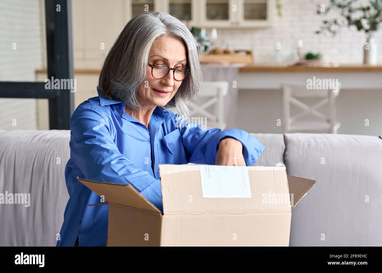 Senior mid age 60s woman opening parcel box at home on the couch Stock ...