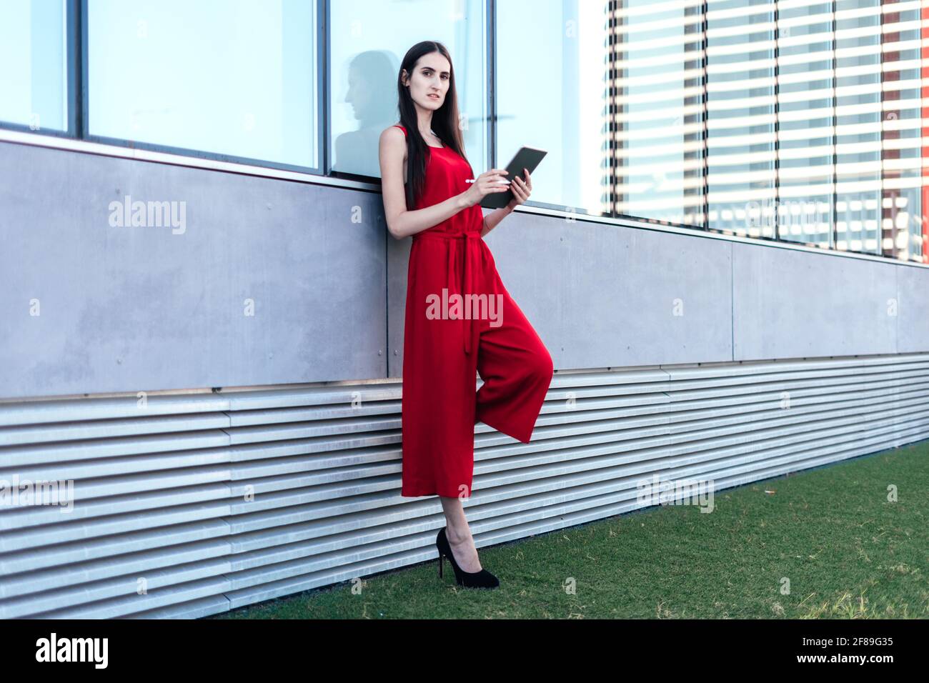 Young caucasian business woman in a red dress writing in her tablet ...