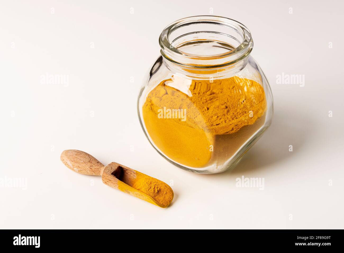 Curry spice powder in glass jar and wooden spoon on white background ...