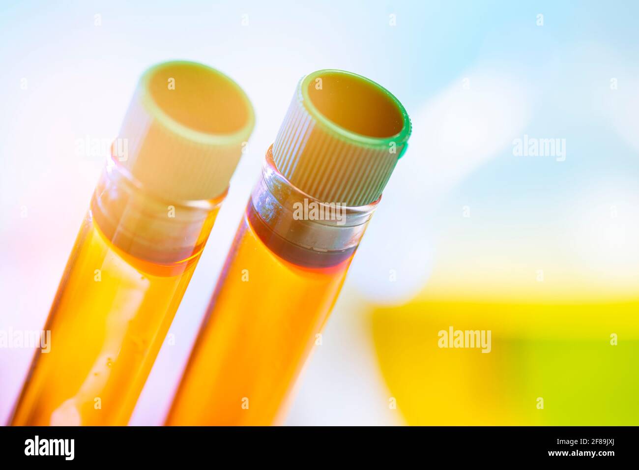 Two chemical test tubes with closed lids with orange liquid on a blue ...