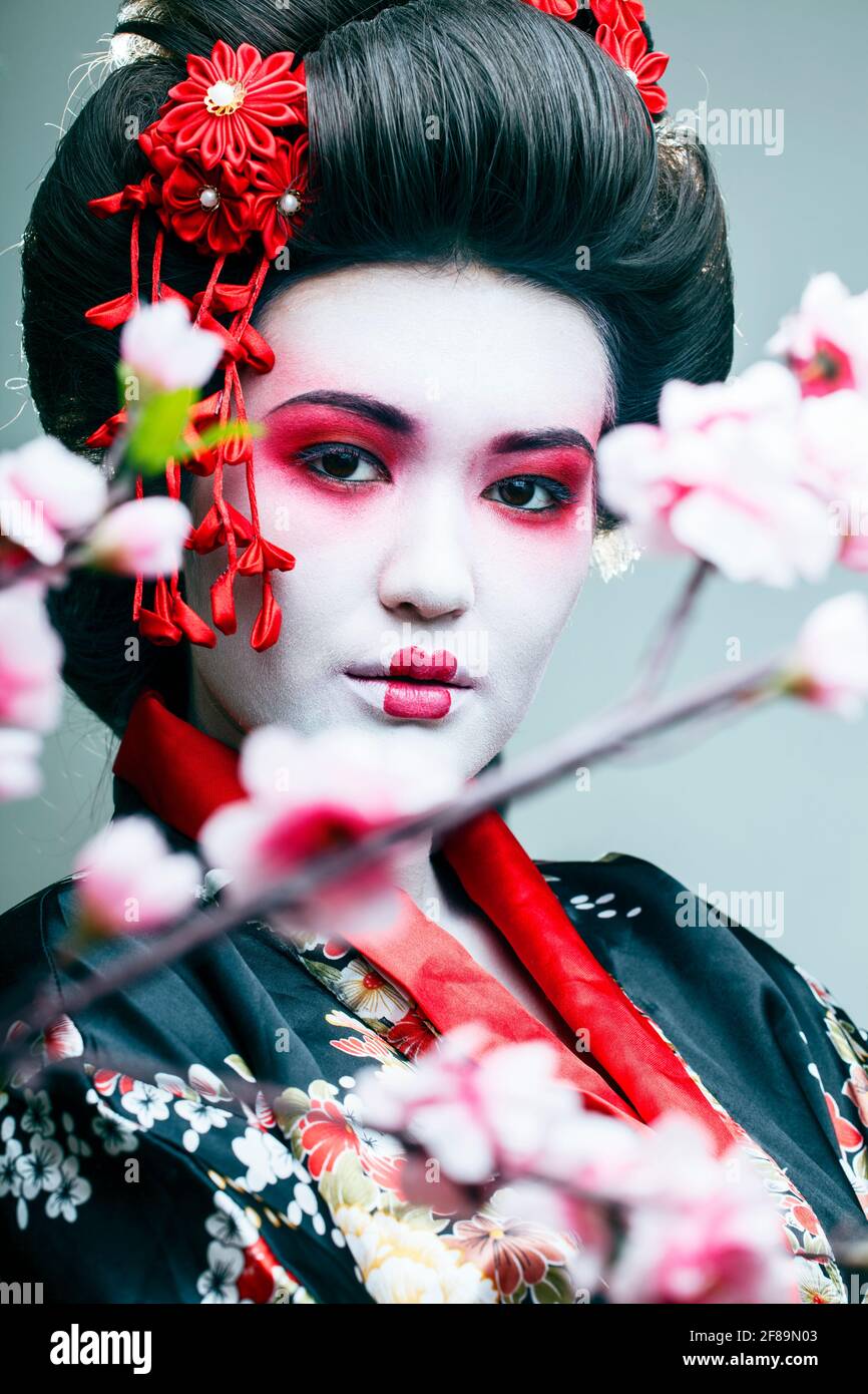young pretty geisha in black kimono among sakura, asian ethno close up ...