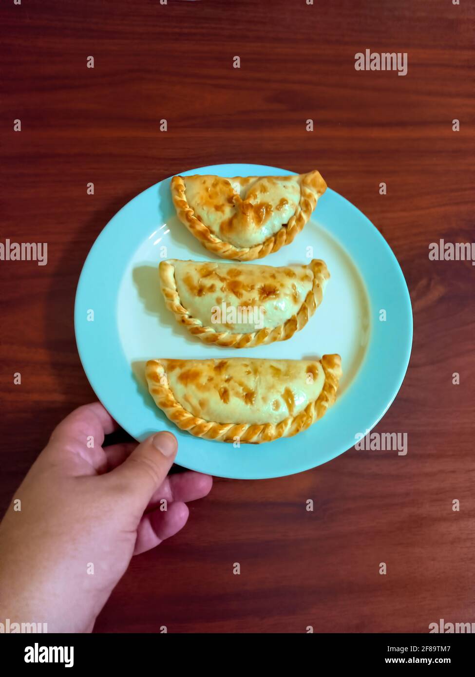 Traditional Argentine baked empanadas on plate held by a hand. Meat ...