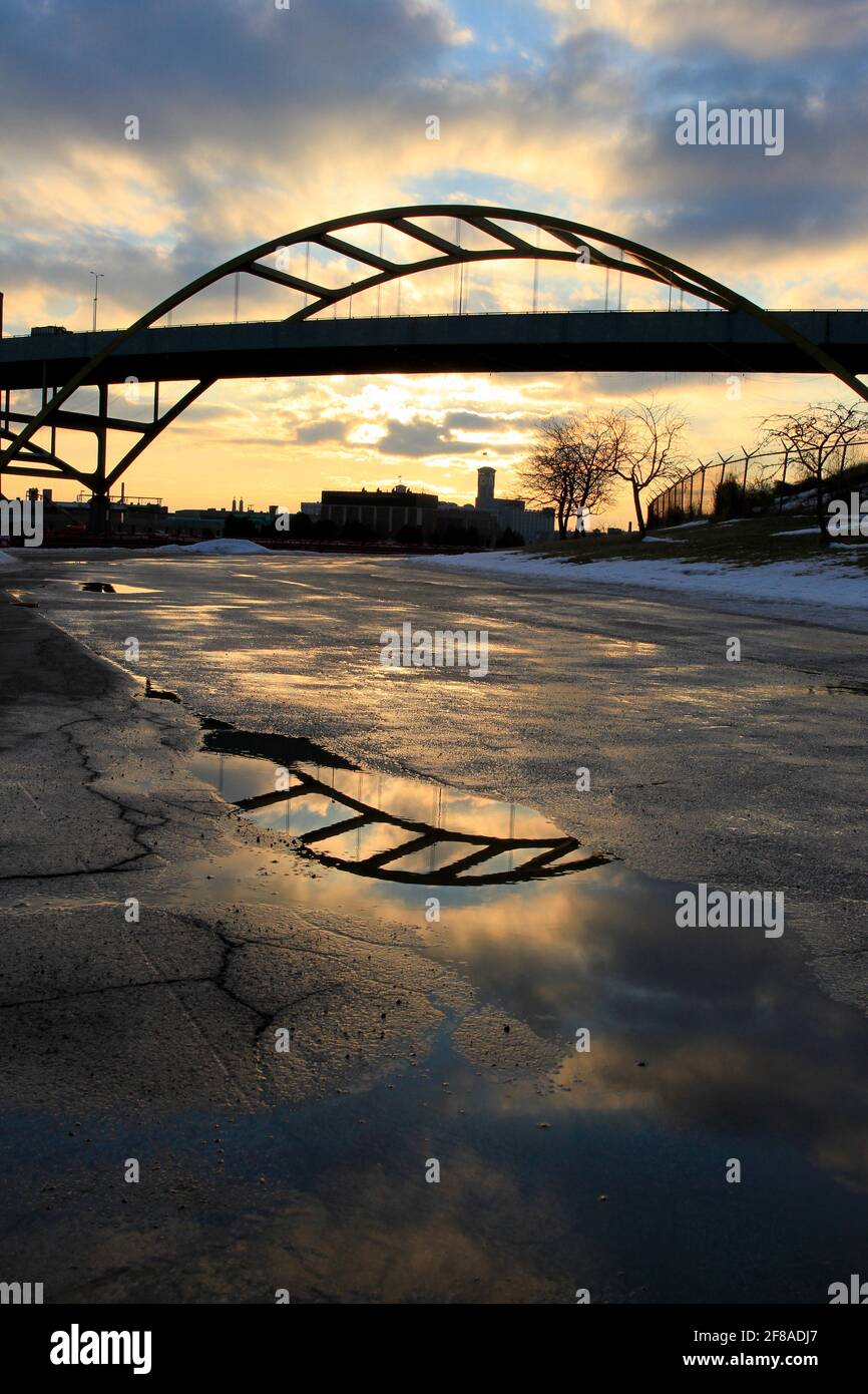 Hone bridge reflected in puddle of water on pavement with sunset behind ...