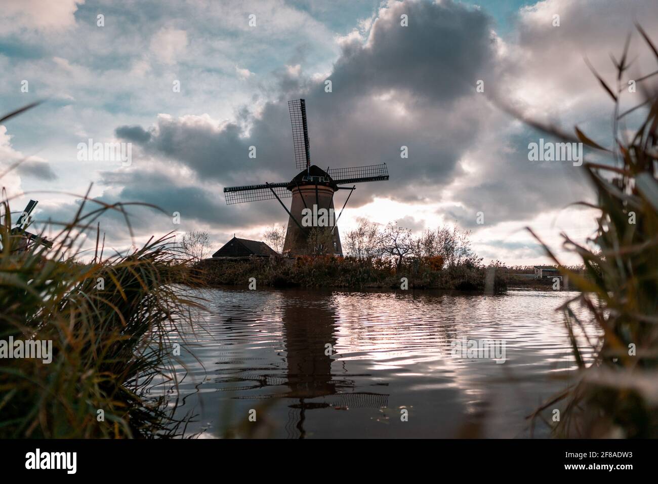 Beautiful shot of a windmill under dense clouds seen through a river ...