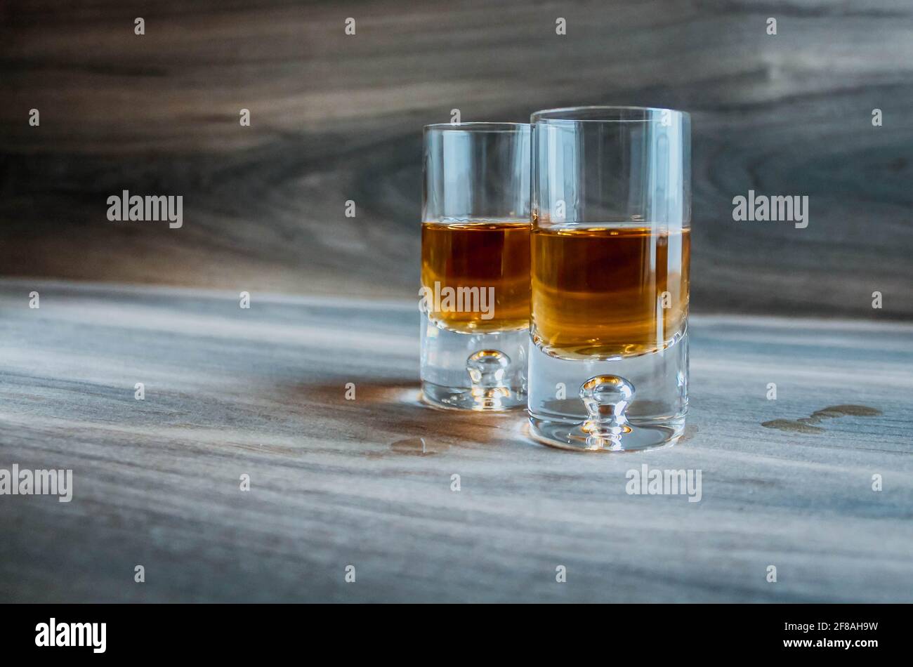 Two shot glasses with whiskey on a wooden background Stock Photo - Alamy