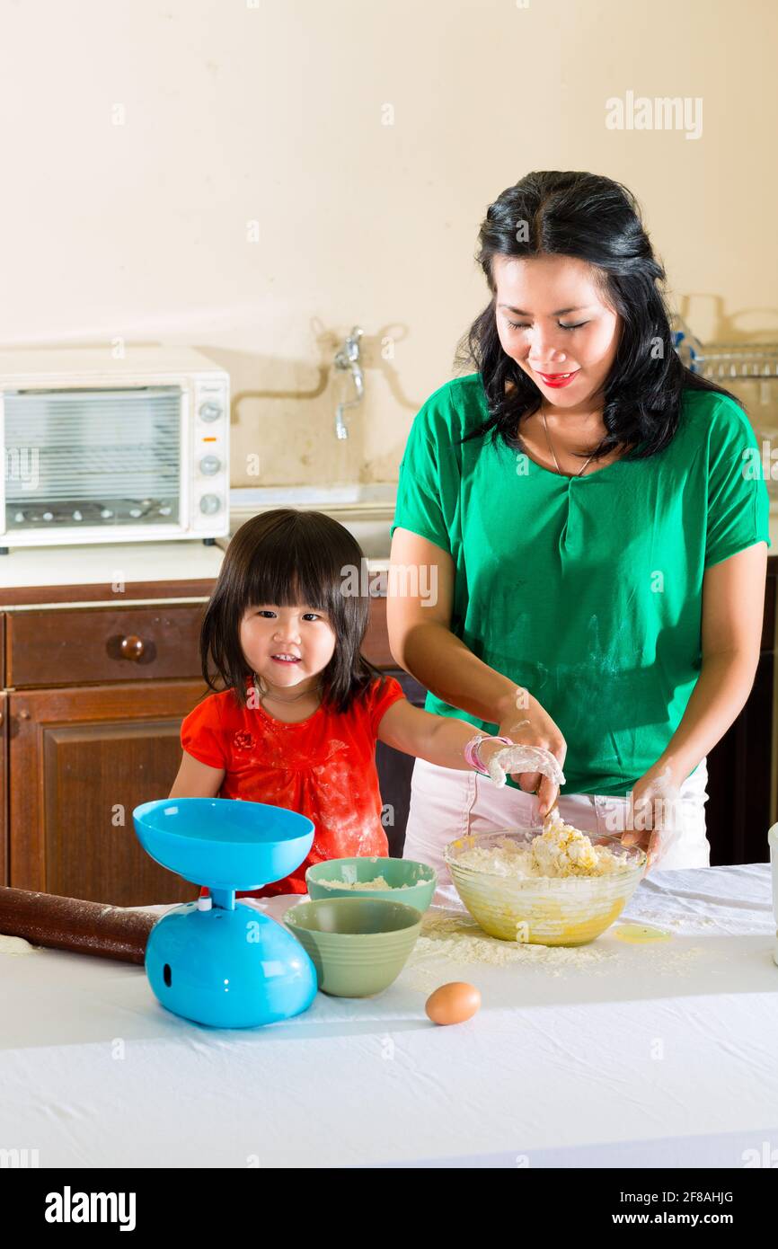 Indonesian Asian Little girl and her mother in the kitchen bake a cake ...