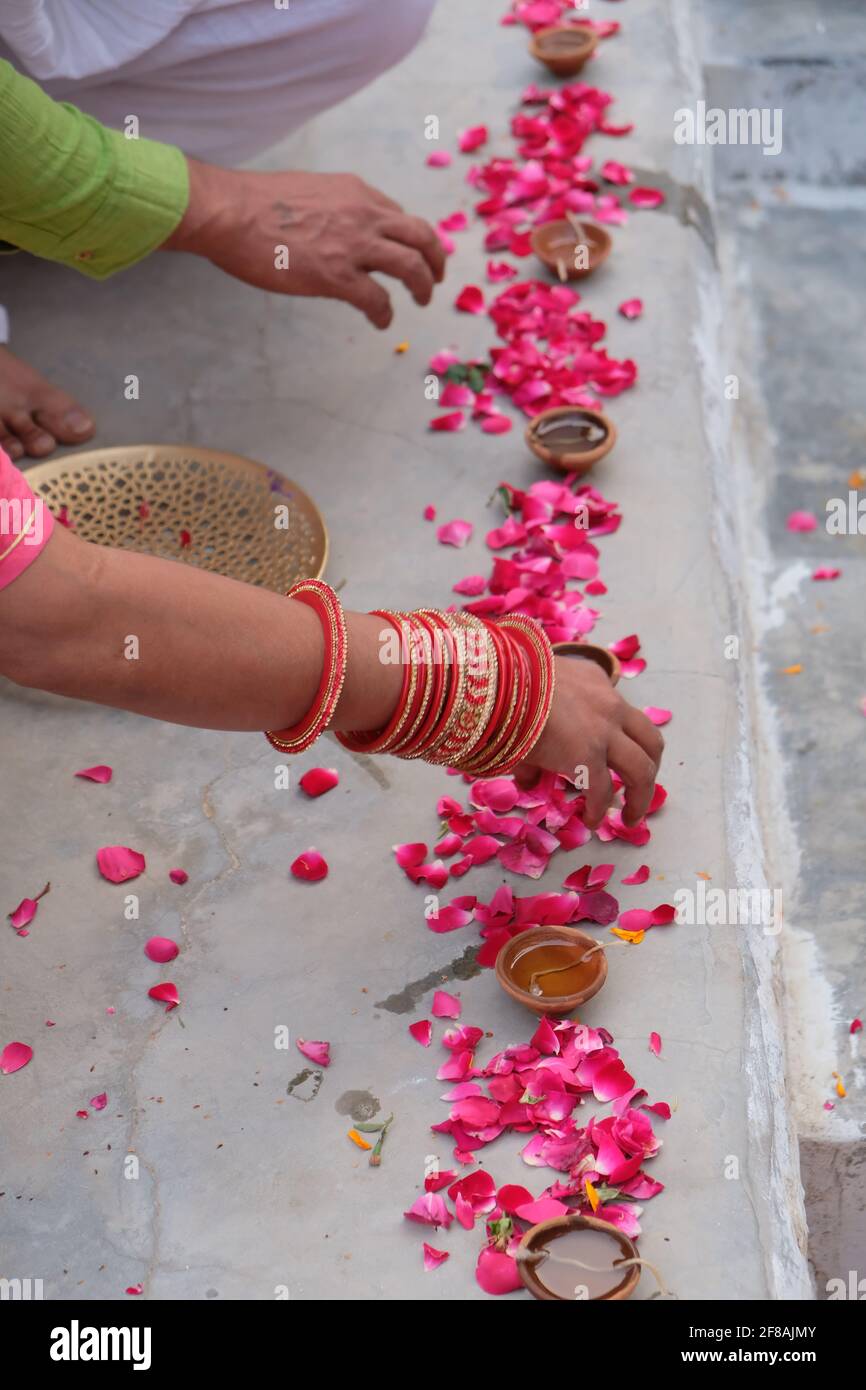 People creating rangoli on the ground with pink rose petals and candles ...