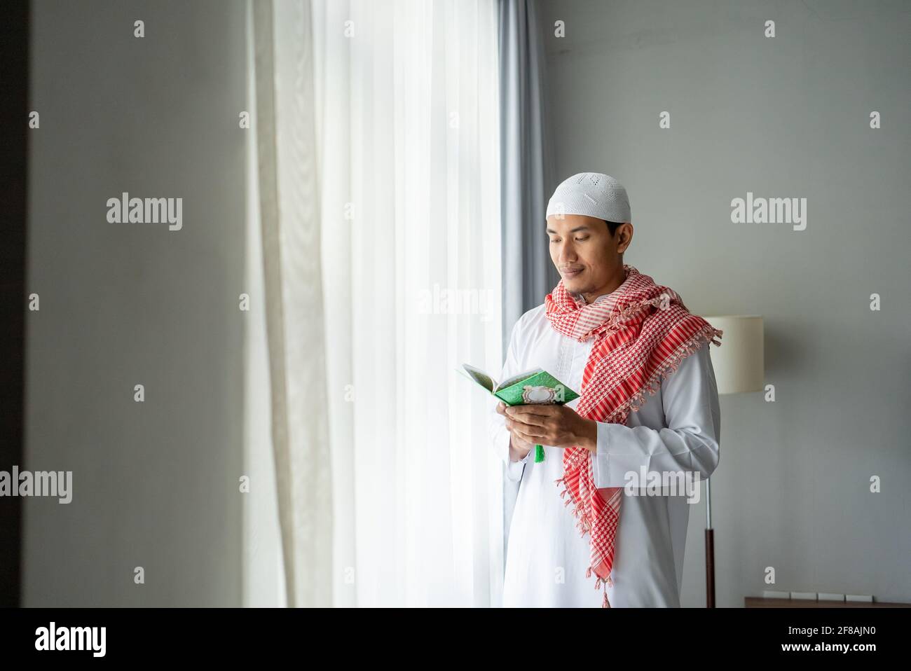 religious man reading koran or quran while standing next to the window ...