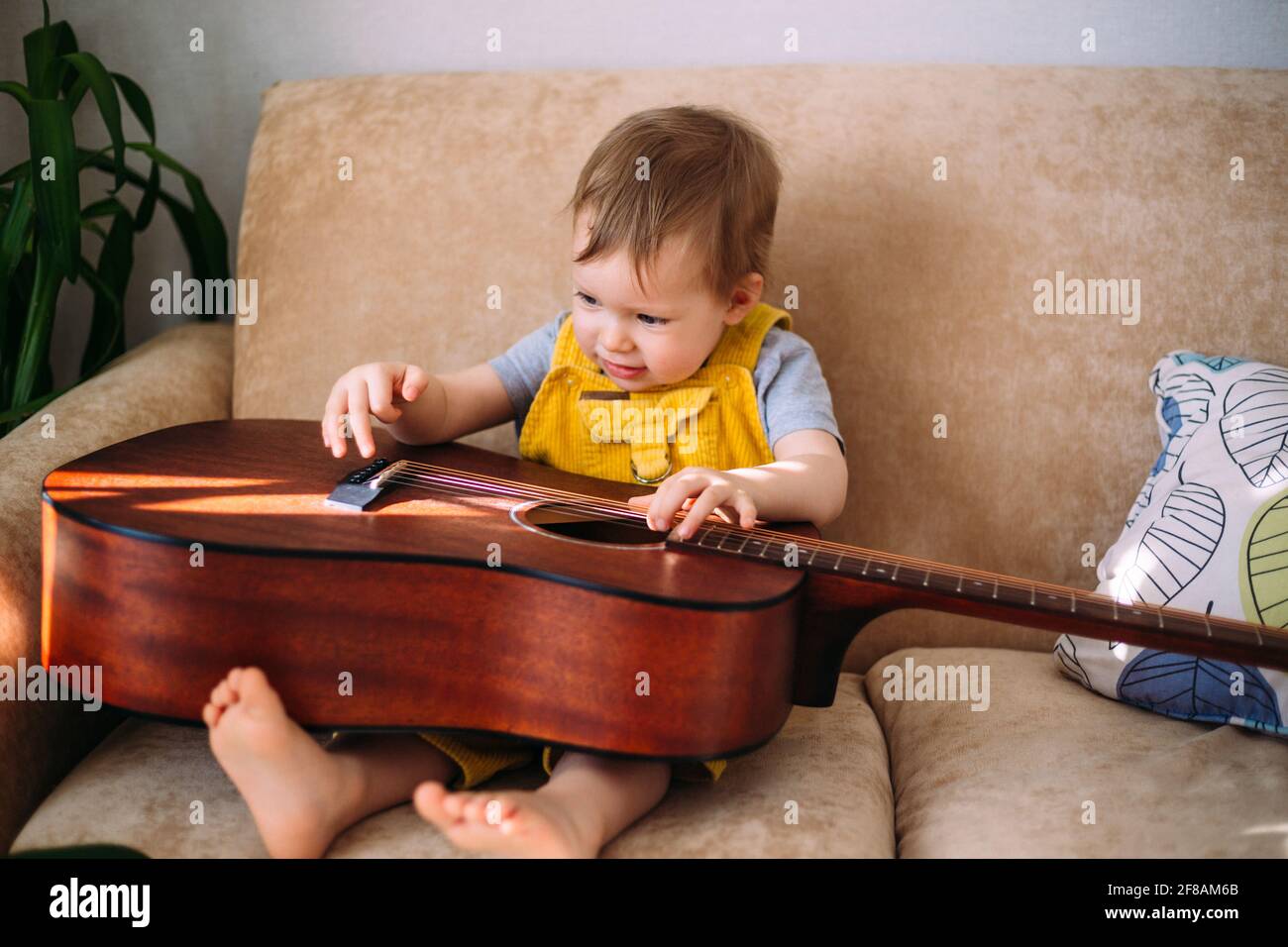 A cute kid plays with a big acoustic guitar at home on the couch Stock ...