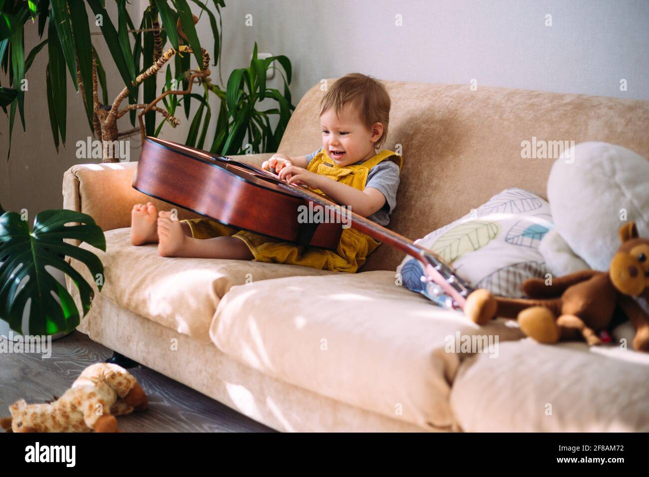 A cute kid plays with a big acoustic guitar at home on the couch Stock ...