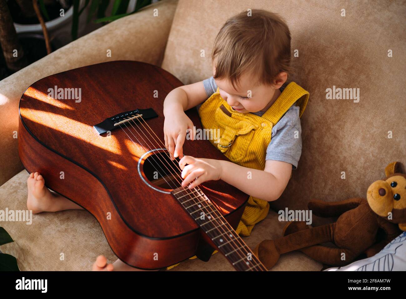 A cute kid plays with a big acoustic guitar at home on the couch Stock ...