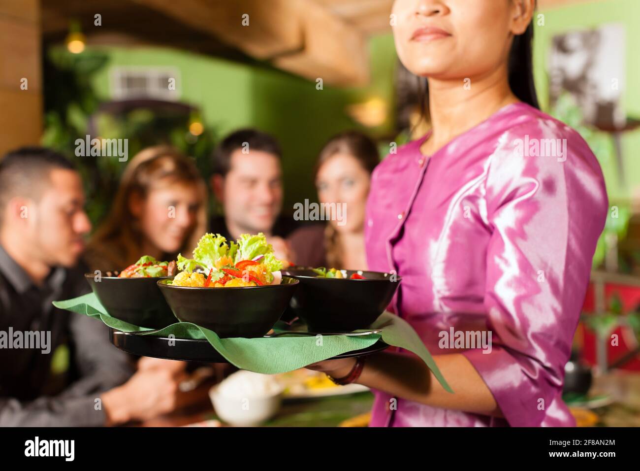 Young people eating in a Thai restaurant; the waitress brings the ...