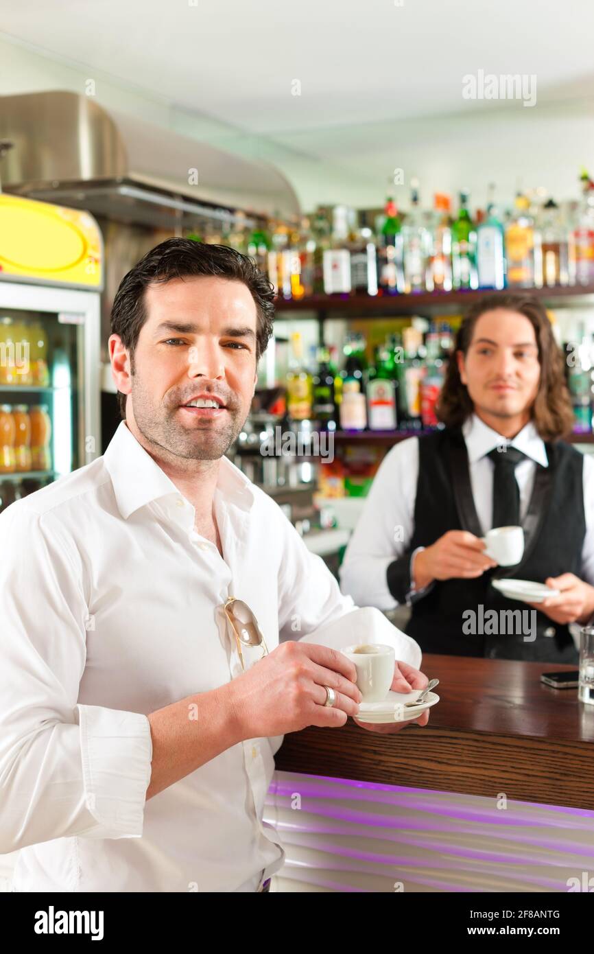 Coffeeshop - barista in cafe with a client, he is drinking coffee, the ...