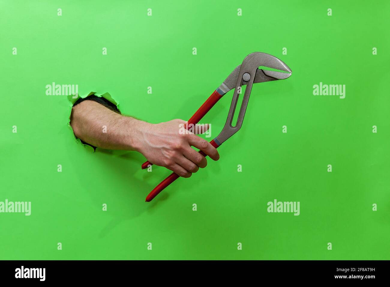 Male hand holds a red pipe key through a torn green paper. Hand through ...