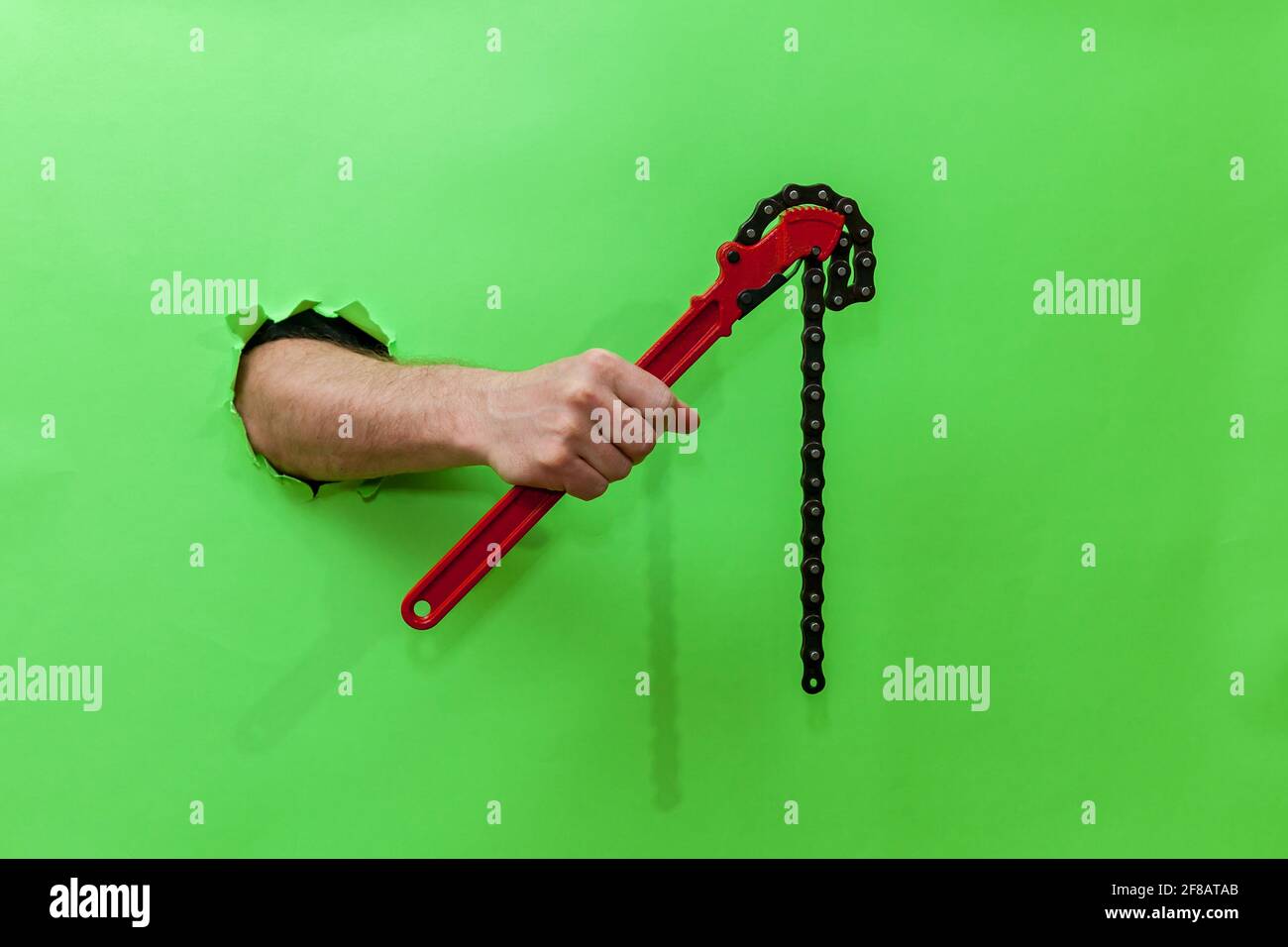 Male hand holds a red pipe key through a torn green paper. Hand through ...