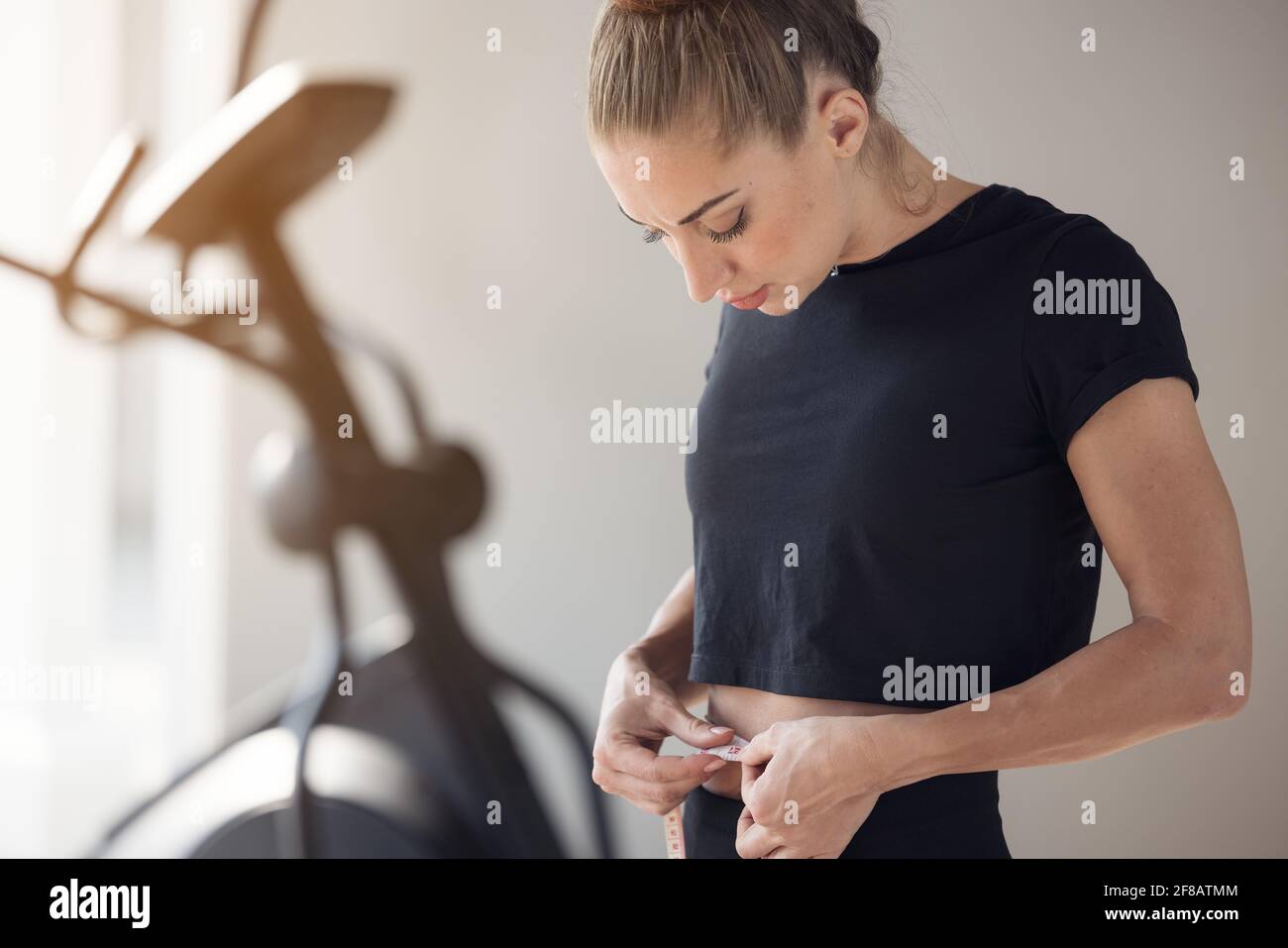 Beautiful fitness model with slim body measures the waist in a fitness ...