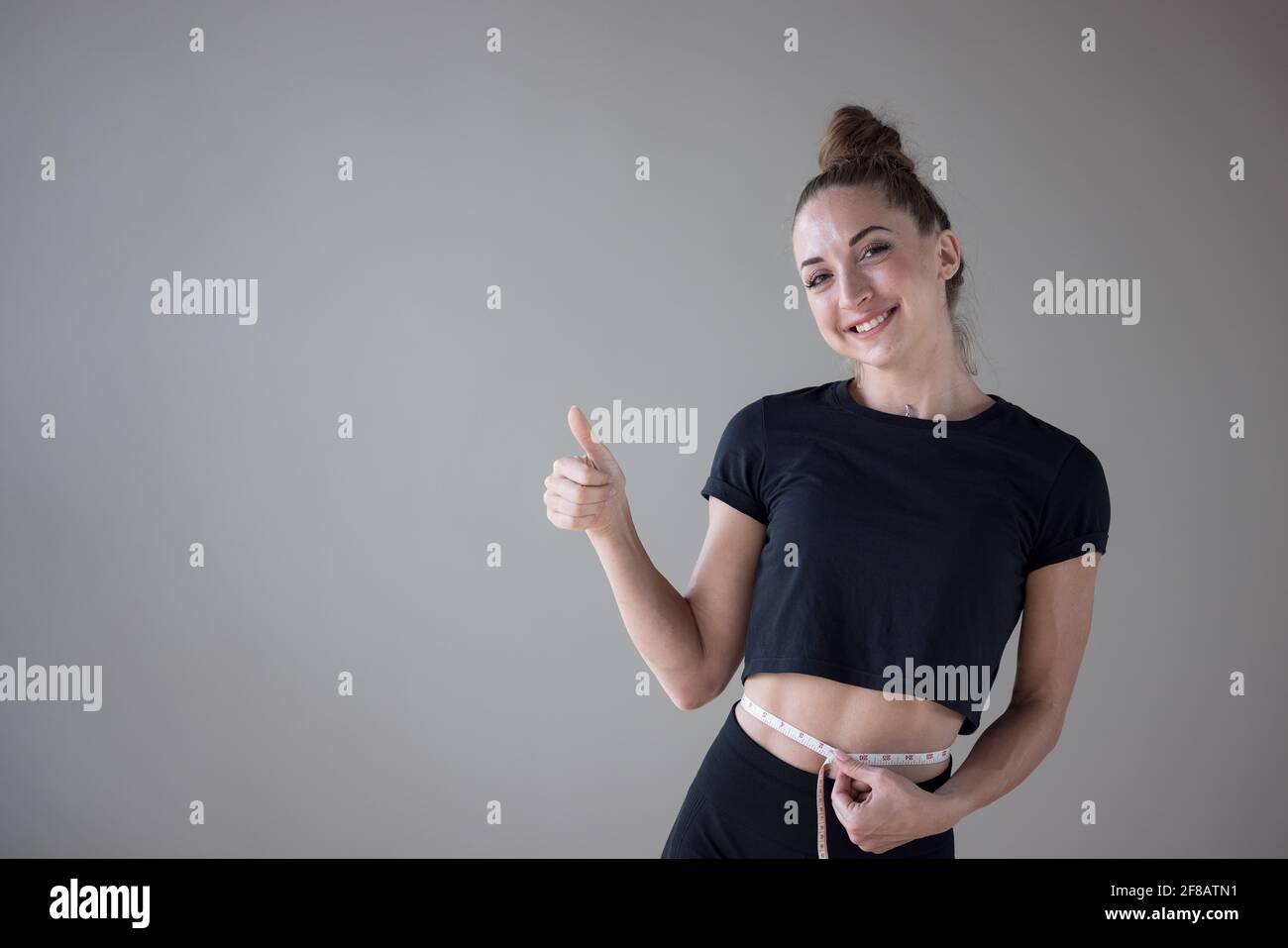 Beautiful fitness model with slim body measures the waist in a fitness ...