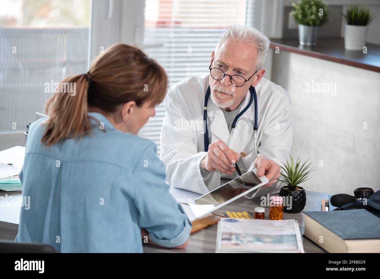 Senior doctor showing reports on digital tablet to his female patient ...