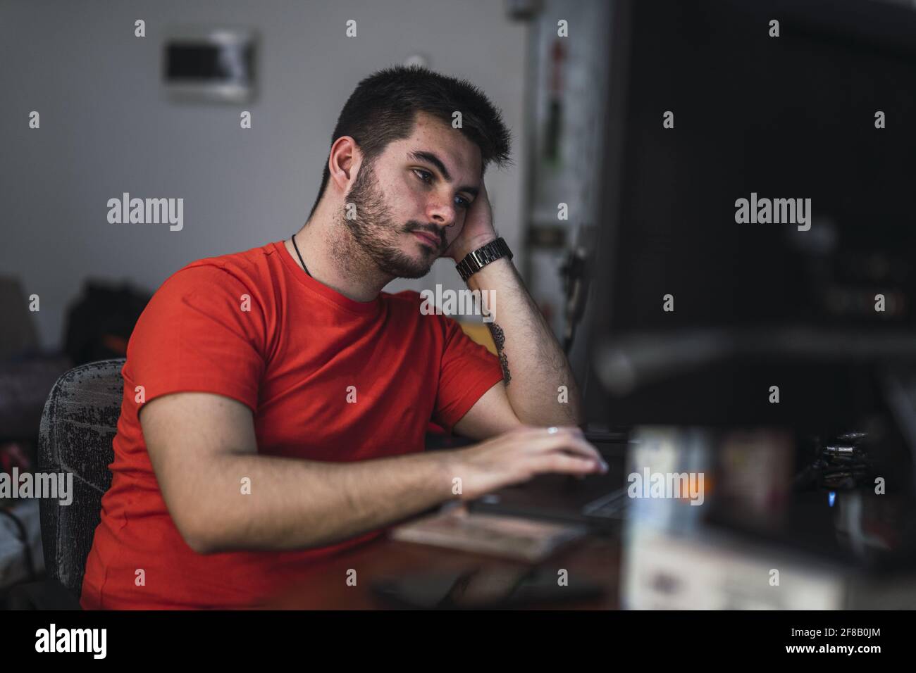 Shallow focus of a bored Caucasian man working on his computer at home ...