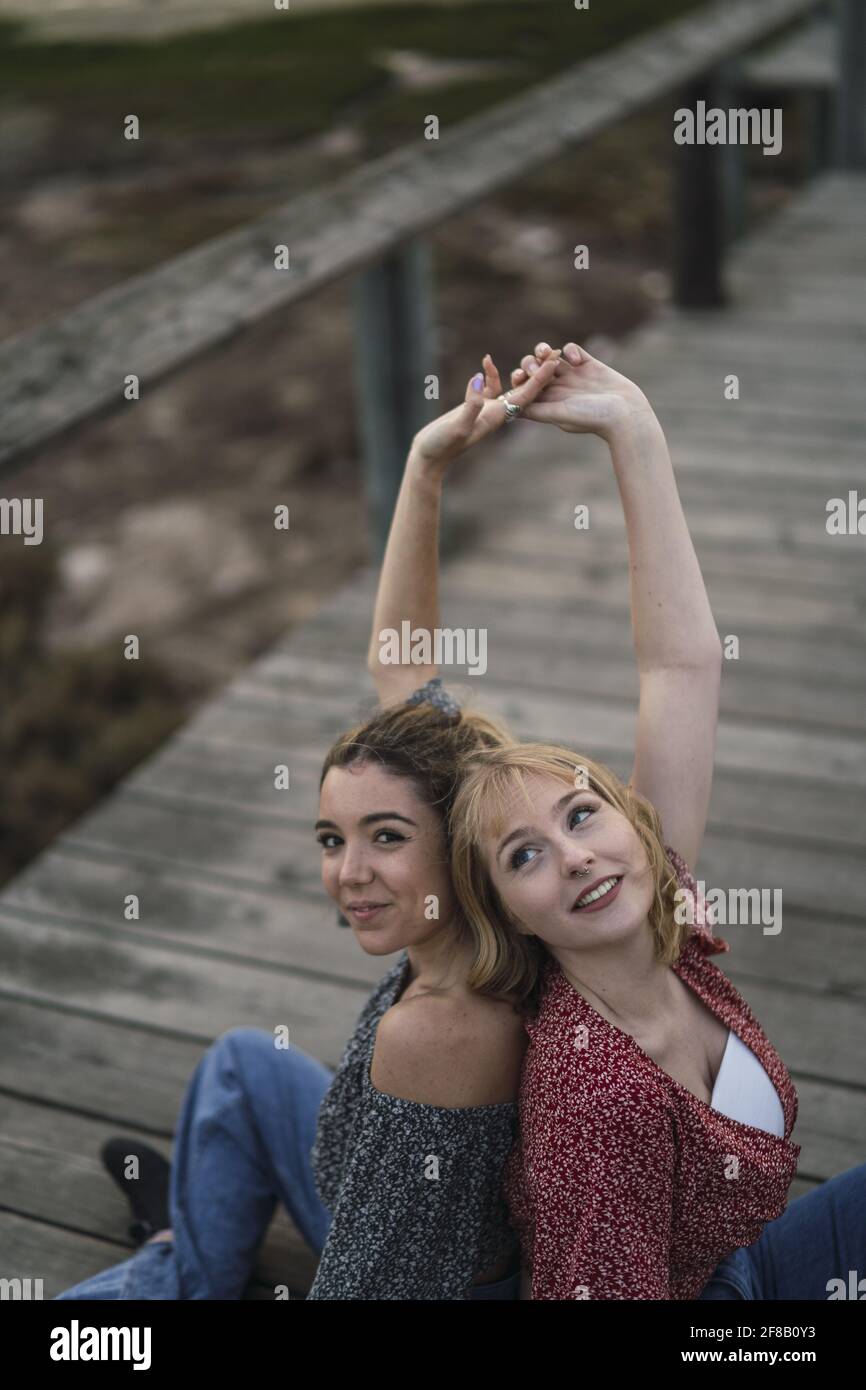 Shallow focus of two female friends sitting on a wooden deck and ...