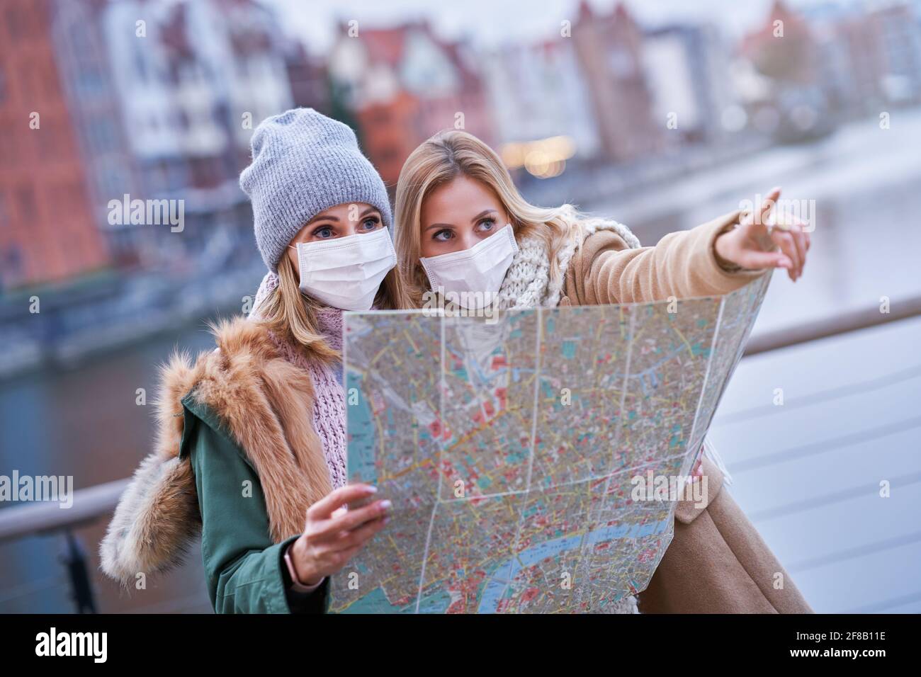 Two women wearing masks and holding map while sightseeing Gdank in ...
