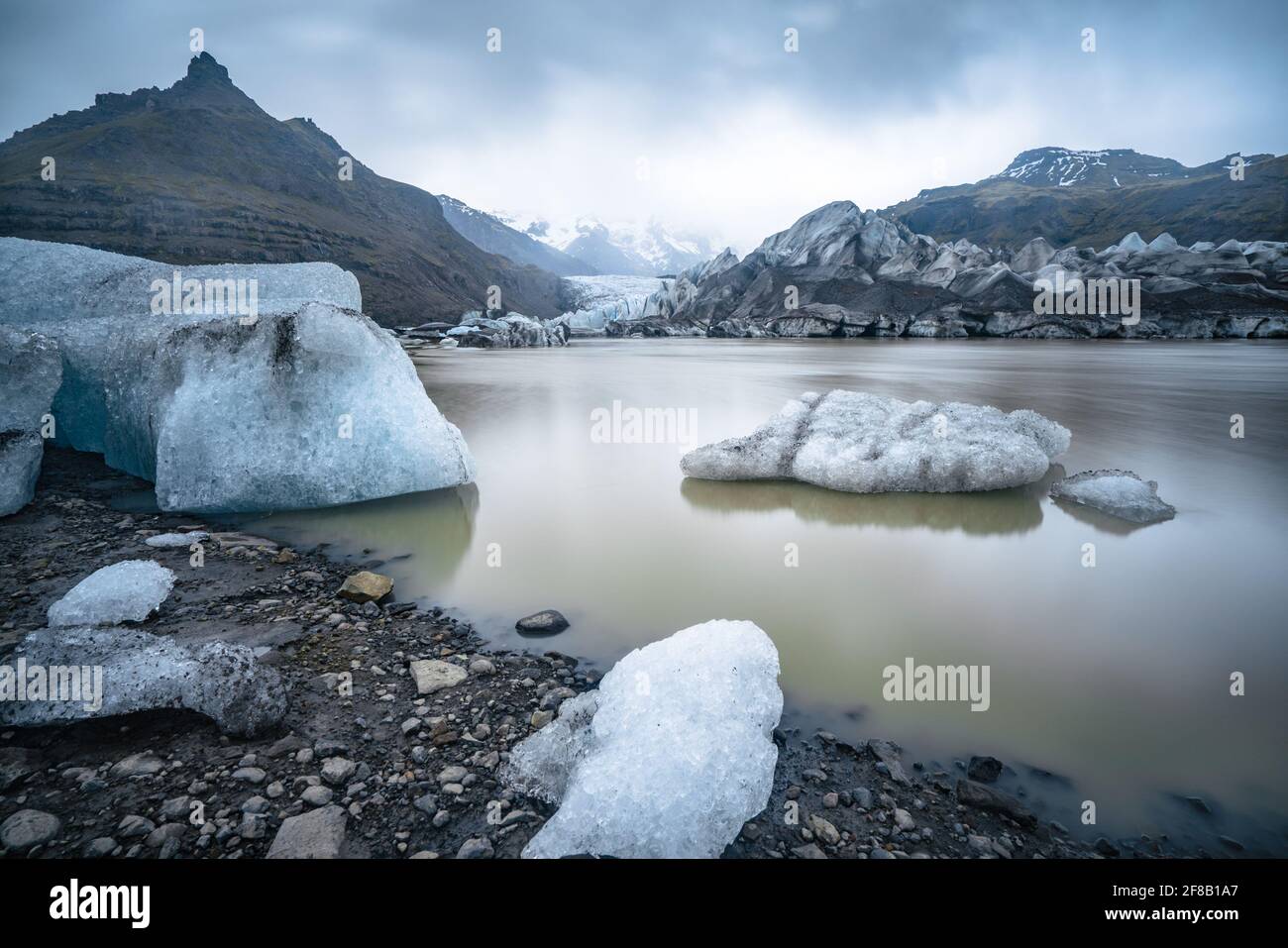 Ice floating in muddy waters of glacier lake with glacier in background ...